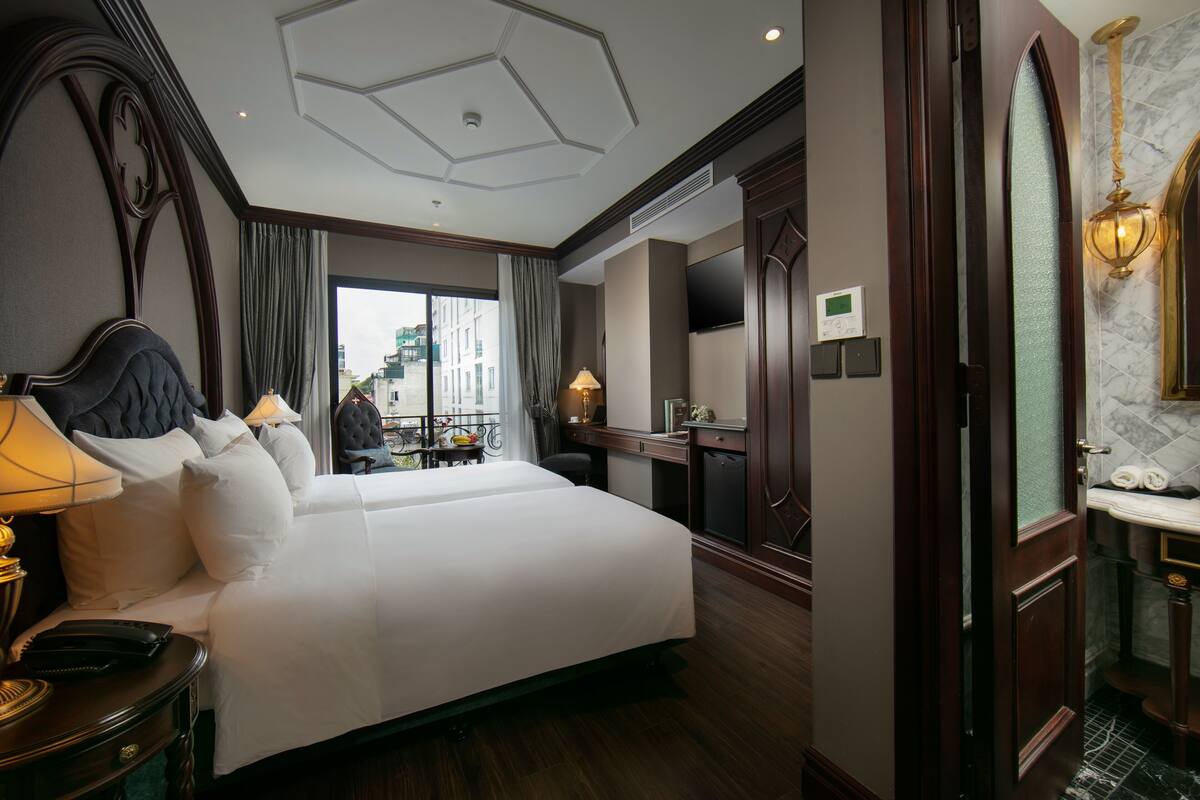 Quarto de hotel com uma cama grande, uma escrivaninha, uma cadeira, televisão e banheiro com espelho e pia.