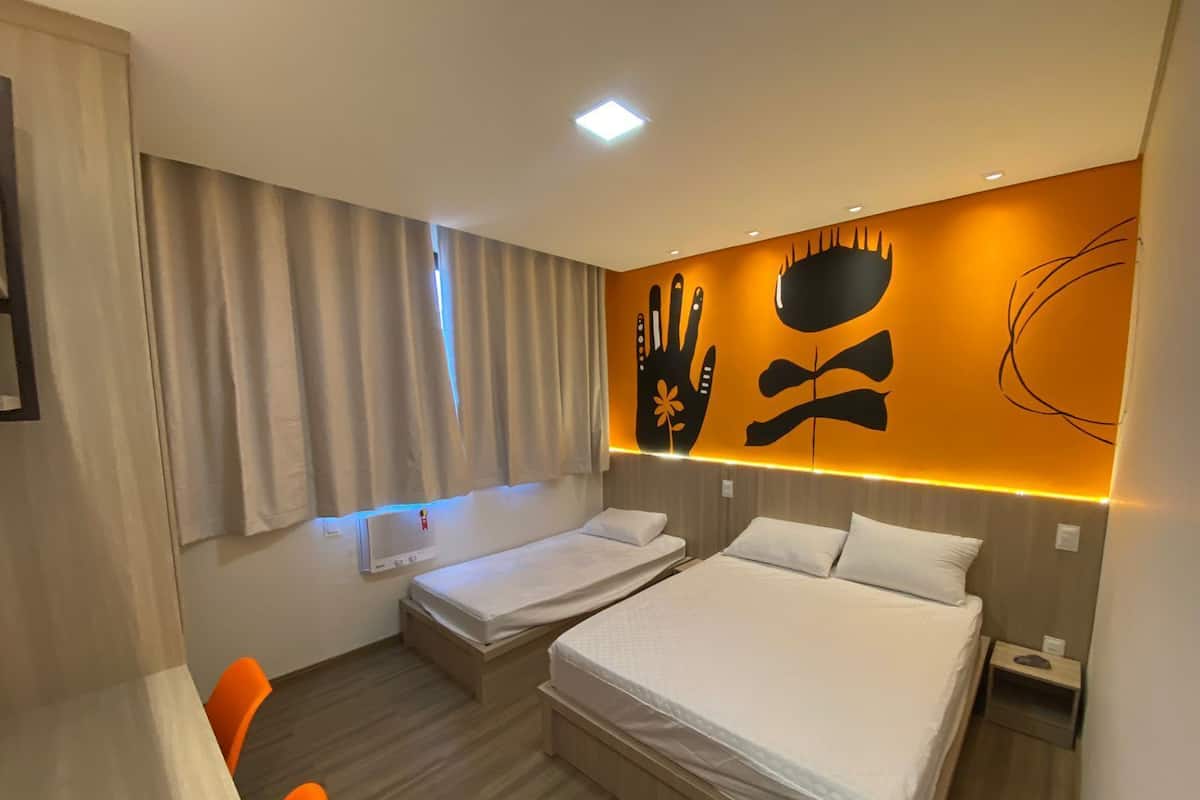 Quarto de hotel com duas camas, uma escrivaninha e uma cadeira.