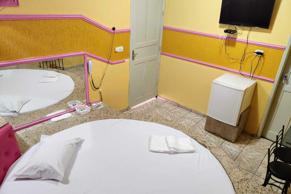 Quarto de hotel com duas camas, televisão, mini-geladeira e uma cadeira.