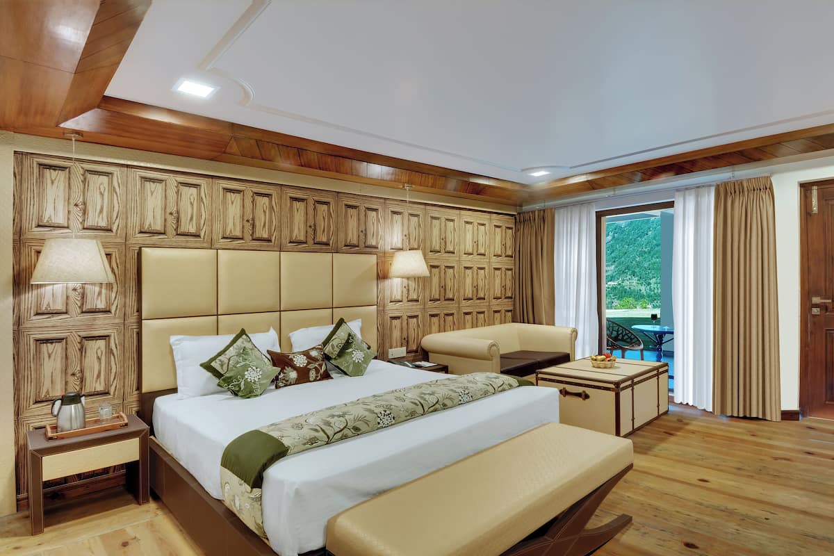 Quarto de hotel com uma cama grande, um sofá, uma mesinha e vista para o exterior.