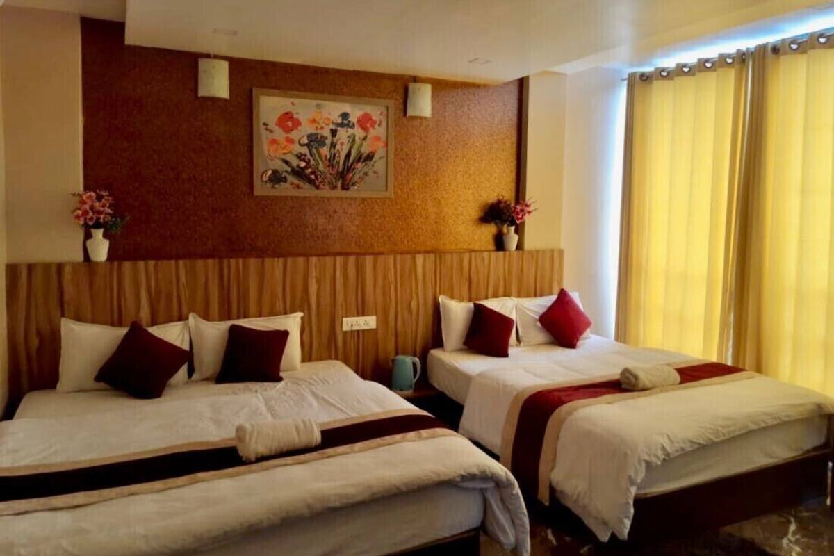 Quarto de hotel com duas camas, cabeceira de madeira, um quadro na parede e uma janela com cortinas.