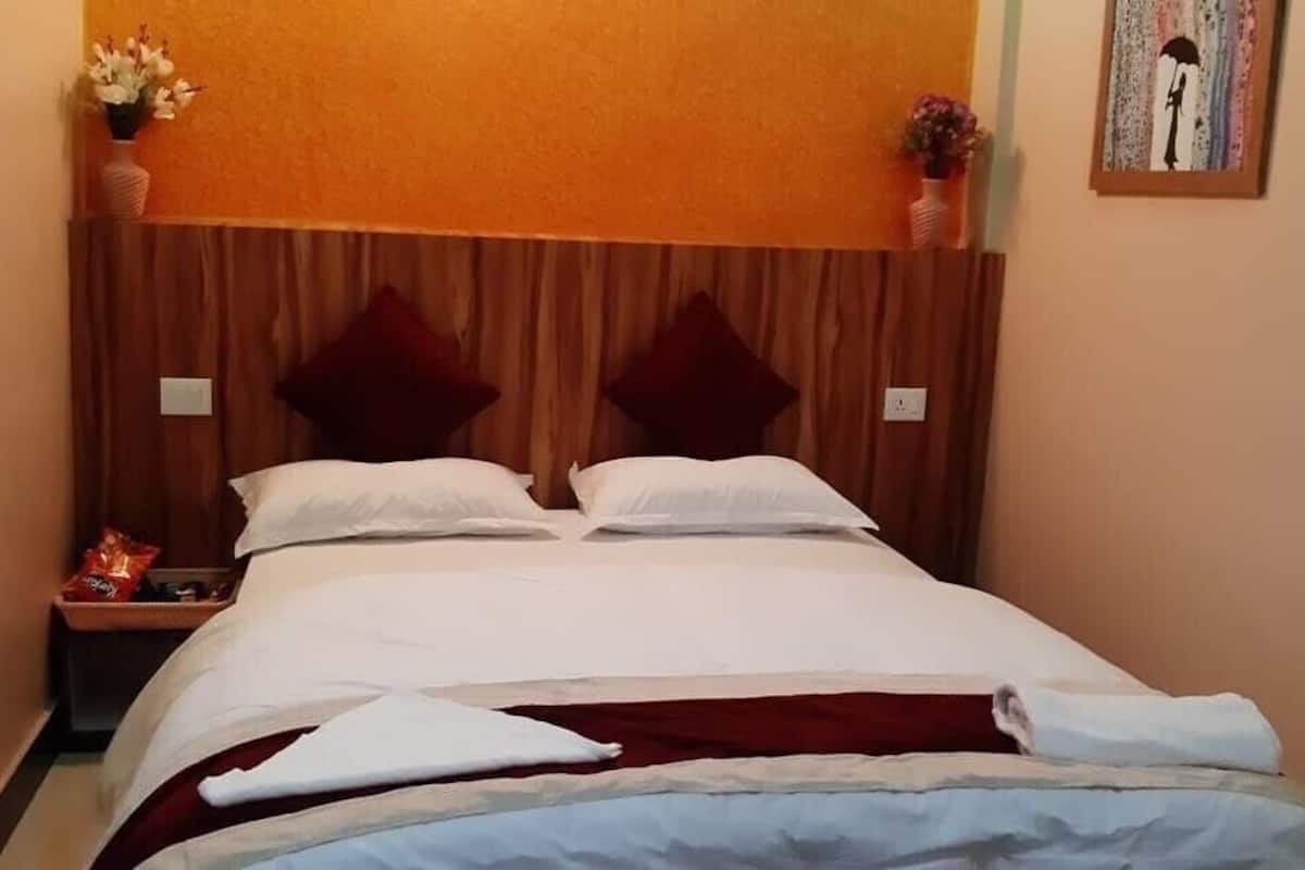 Uma cama bem arrumada com lençóis brancos e um cobertor vermelho, uma cabeceira de madeira e uma mesa de cabeceira com um vaso de flores.