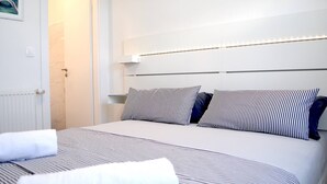 Quarto de hotel com cama, porta e cabeceira com iluminação embutida.