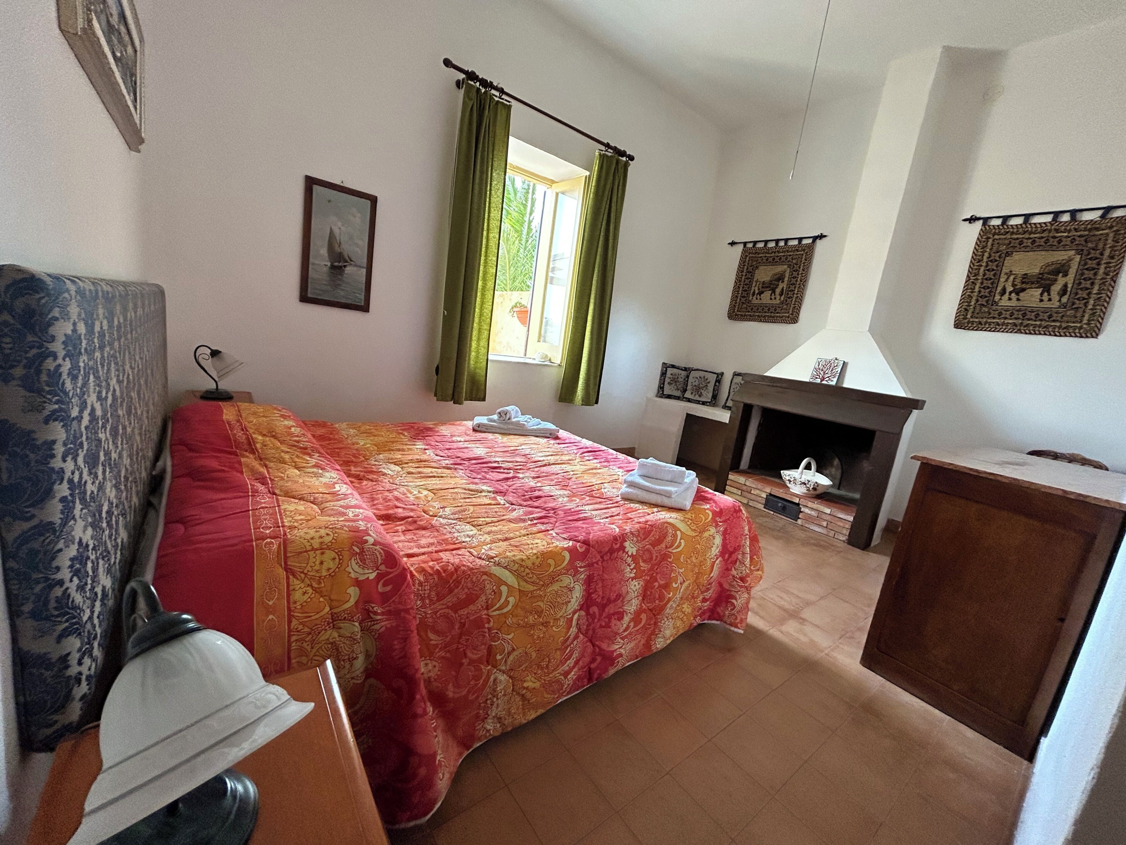 Um quarto com cama, poltrona, lareira e janela com cortinas.