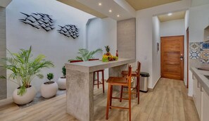 Uma cozinha moderna com ilha central, cadeiras de madeira, plantas em vasos e detalhes decorativos nas paredes.