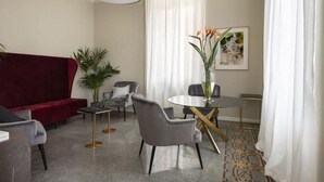 Uma sala de estar moderna com um sofá vermelho, poltronas cinzas, uma mesa redonda com um vaso de flores e uma grande janela com cortinas translúcidas.
