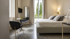 Quarto de hotel moderno com cama, escrivaninha, cadeira, televisão e varanda com vista para árvores.