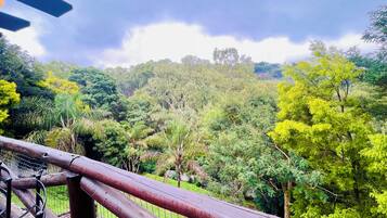 Vista de uma varanda com guarda-corpo de madeira, com vista para uma floresta verdejante e uma colina ao longe.