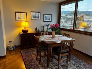 Uma área de refeições com mesa de madeira, cadeiras, tapete estampado, luminária e quadros nas paredes.