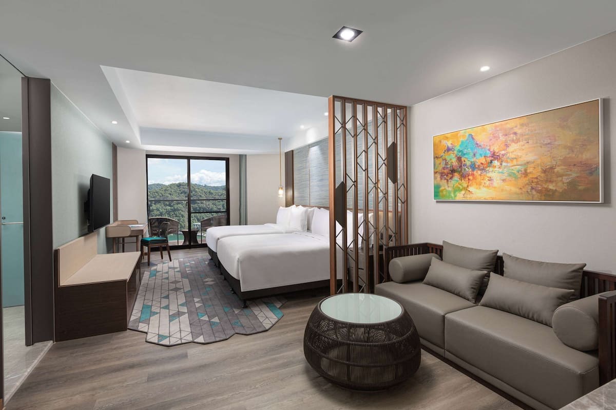 Quarto de hotel moderno com uma cama grande, um sofá, uma mesa de centro redonda e uma televisão.