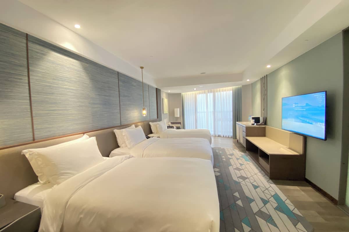 Quarto de hotel com duas camas, uma escrivaninha, televisão e uma janela grande com cortinas.