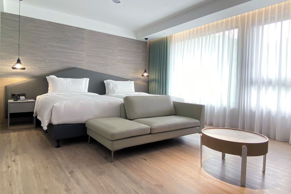 Quarto de hotel moderno com uma cama grande, um sofá, uma mesinha e uma mesadinha de cabeceira.
