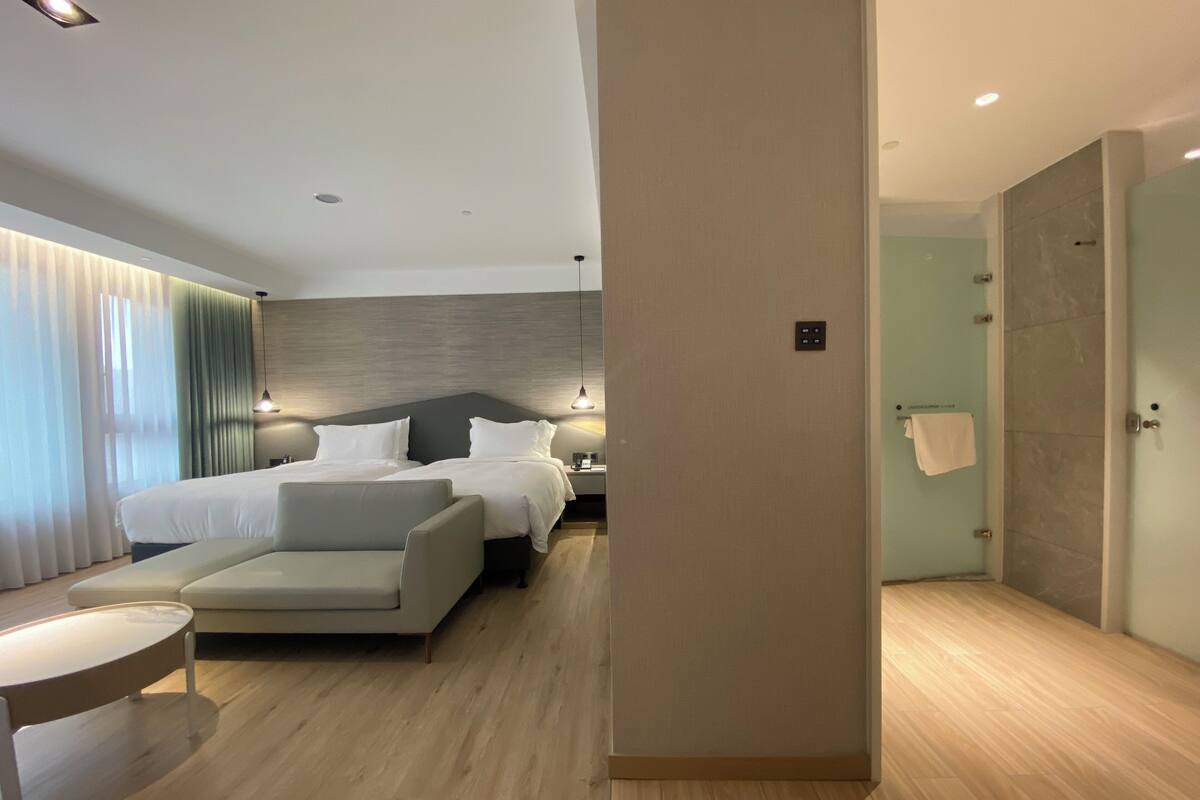 Quarto de hotel moderno com uma cama, um sofá, uma mesinha e zona de duche.