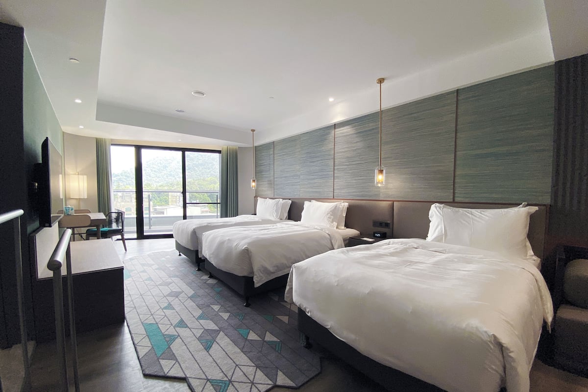 Quarto de hotel moderno com duas camas, uma escrivaninha e uma televisão.