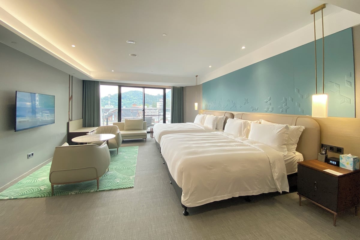 Quarto de hotel com uma cama grande, uma escrivaninha, uma cadeira e uma televisão.