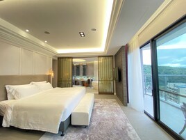 Quarto de hotel moderno com uma cama grande, banheiro com toucador e varanda com vista para a cidade.