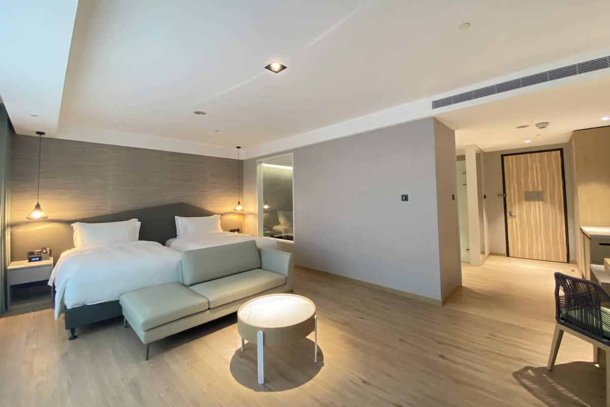 Quarto de hotel moderno com uma cama grande, um sofá, uma mesinha e uma cadeira.