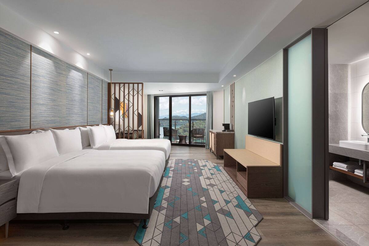 Quarto de hotel moderno com uma cama grande, televisão, escrivaninha e varanda com vista.