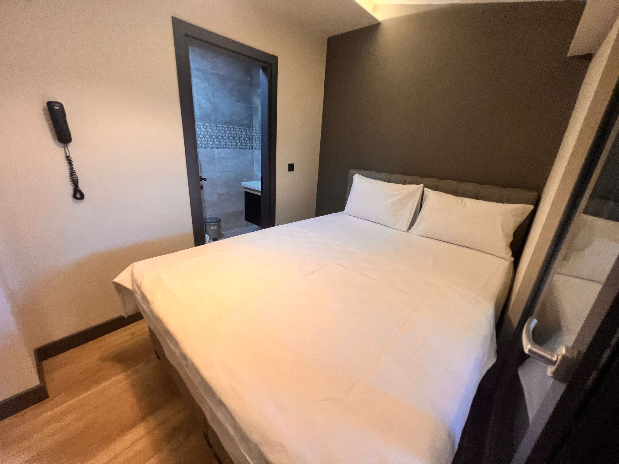 Quarto de hotel com uma cama, um telefone e uma porta para um banheiro.