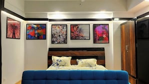 Quarto com sofá azul, ventilador de teto e obras de arte nas paredes.