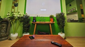 Sala de conferências com tela de projeção exibindo mensagem de atualização de software, mesa de madeira, controle remoto e plantas em vasos.