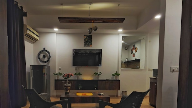 Uma sala de estar moderna com televisão de tela plana, móveis escuros e um objeto decorativo na parede.