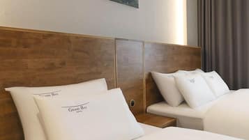 Quarto de hotel com cabeceira de madeira, roupa de cama branca e almofadas com o logotipo do Grand Bay Hotel.