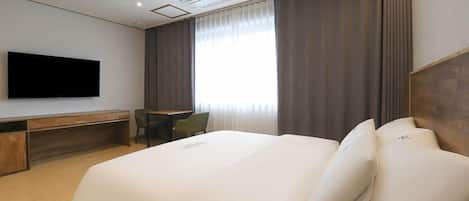 Quarto de hotel com cama grande, escrivaninha, cadeira, televisão de tela plana e janela com cortinas.
