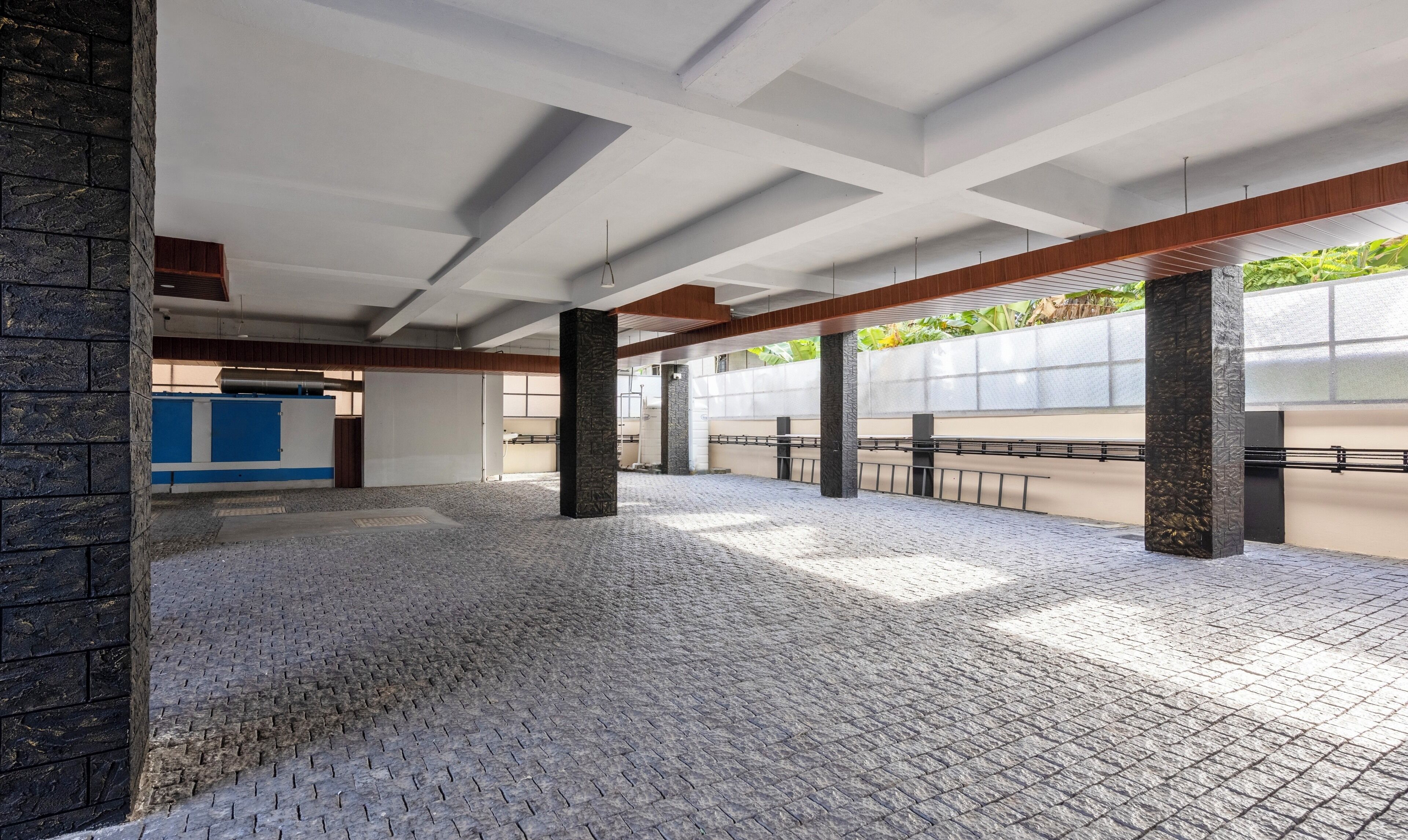 Um espaço interior com soalho em mosaico, pilares imponentes e teto alto com vigas aparentes.