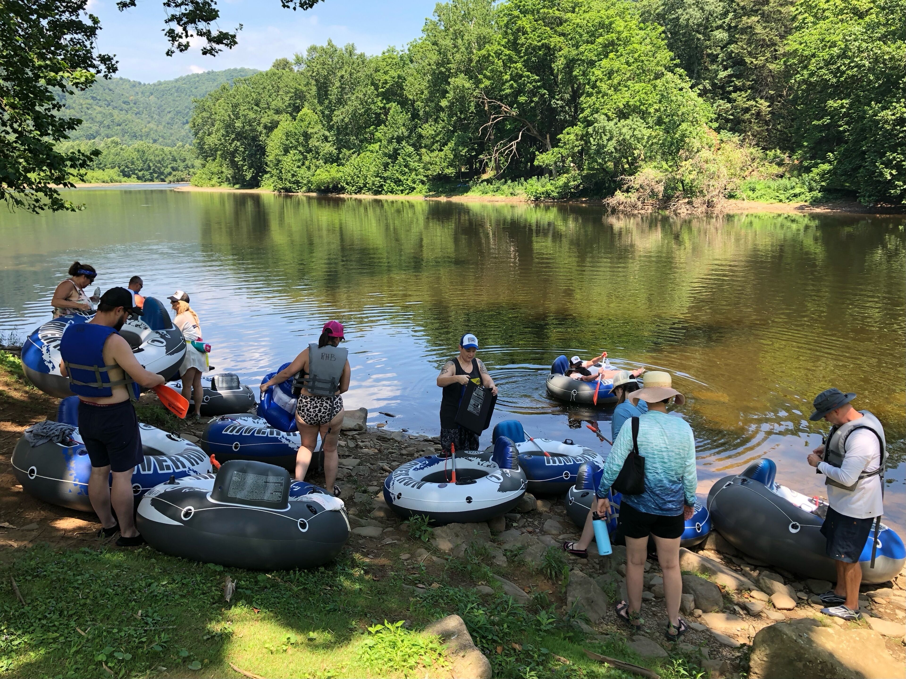 Um grupo de pessoas se preparando para uma aventura de rafting em um rio calmo, cercado por vegetação exuberante.