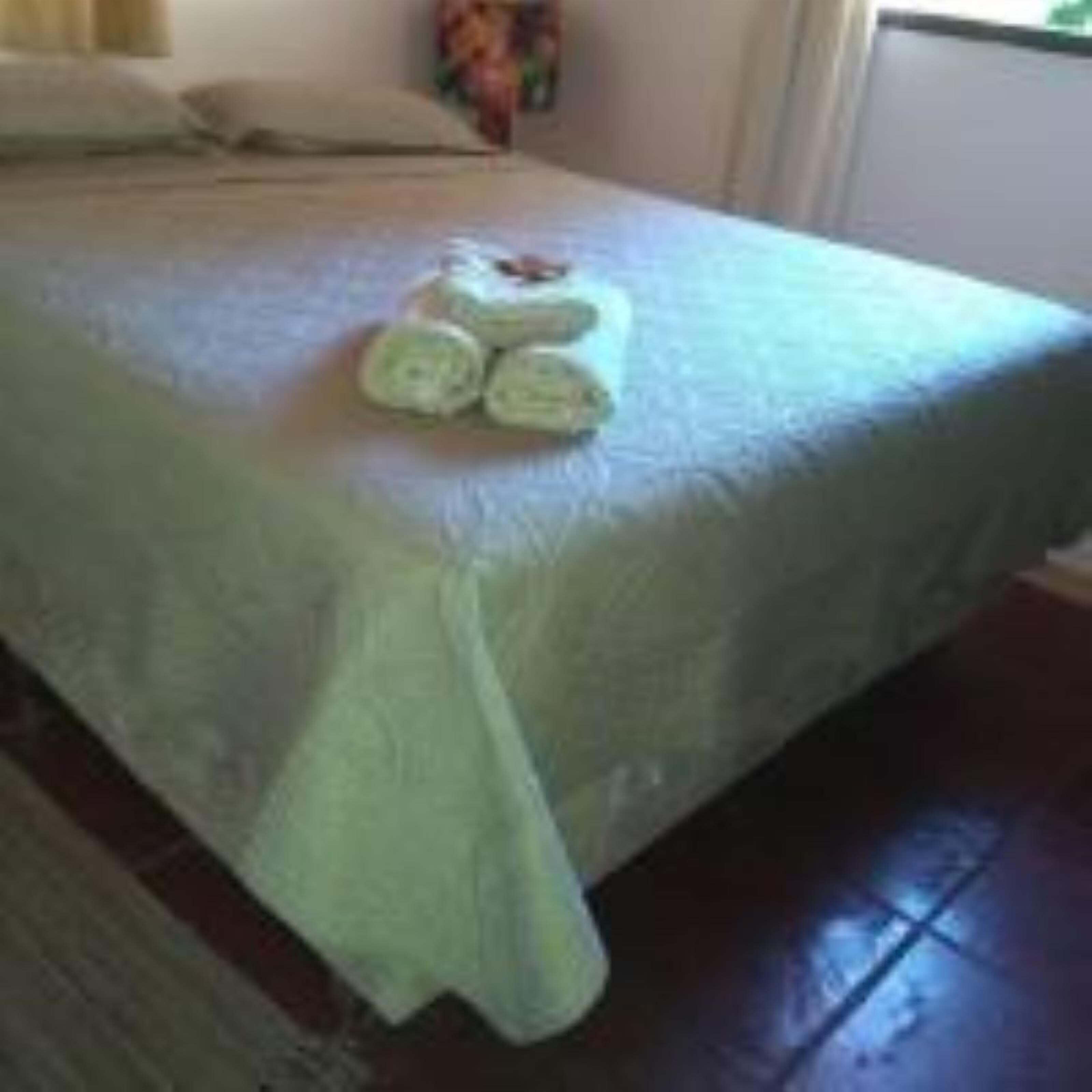 Cama com colcha verde e duas toalhas enroladas.