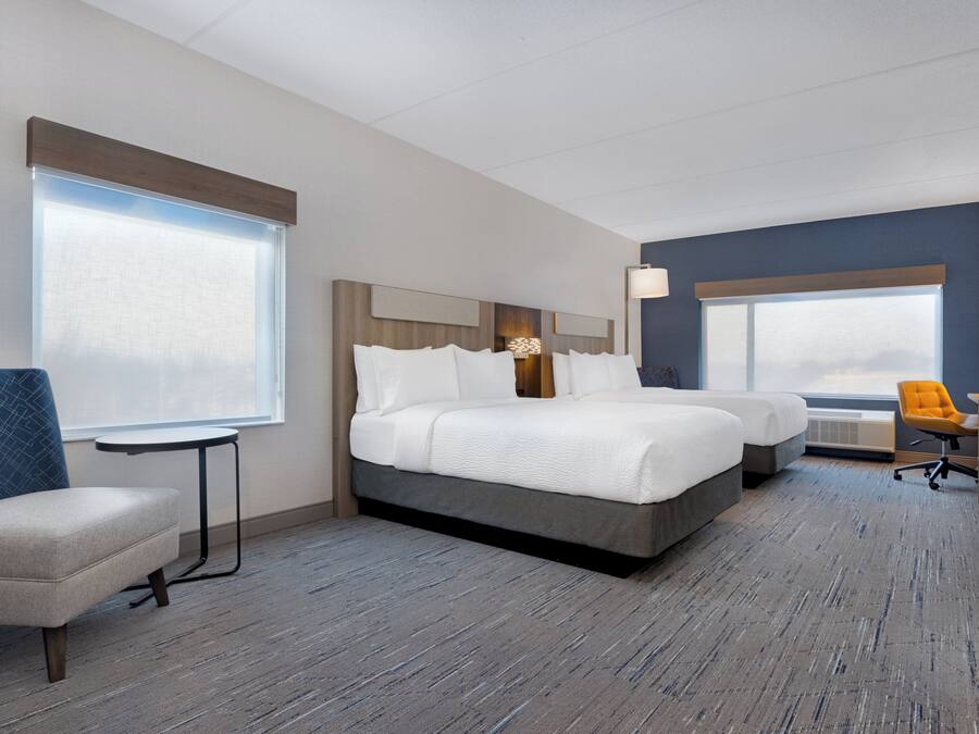 Quarto de hotel com uma cama grande, uma cama menor, uma escrivaninha, uma cadeira e uma janela.