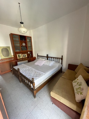 Um quarto com cama de madeira, guarda-roupa de madeira, mesa de cabeceira e um sofá.