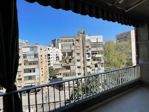 Uma varanda com vista para prédios residenciais, uma rua e algumas áreas verdes.