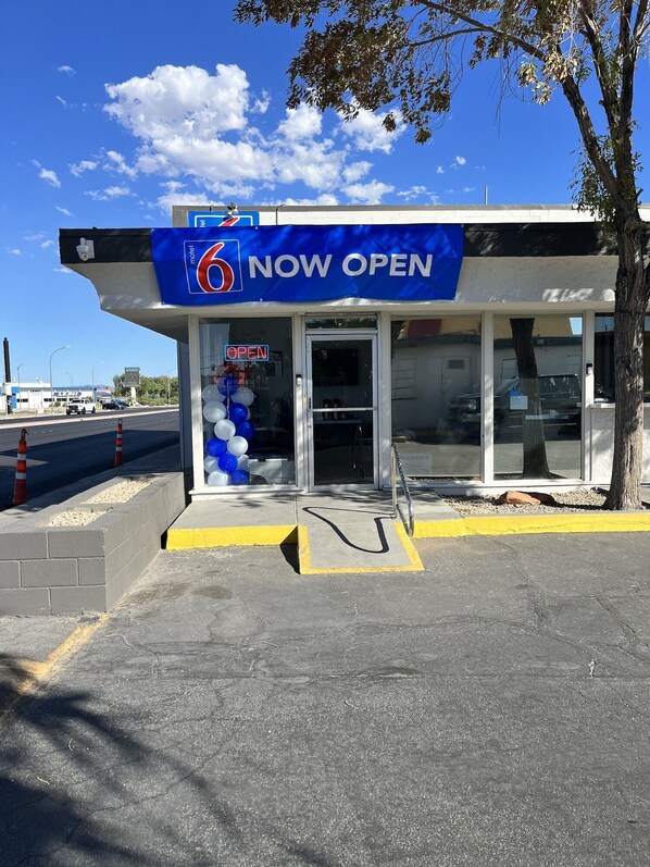 Um motel com uma placa azul que diz “6 ABERTURA AGORA” e uma entrada de vidro.