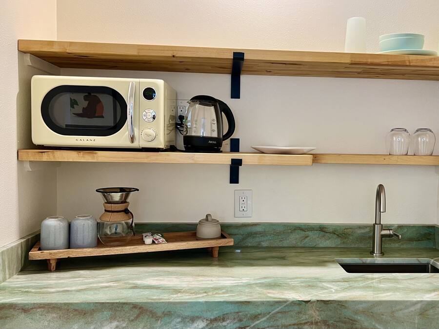 Cozinha equipada com micro-ondas, chaleira e prateleira com louça e frascos.