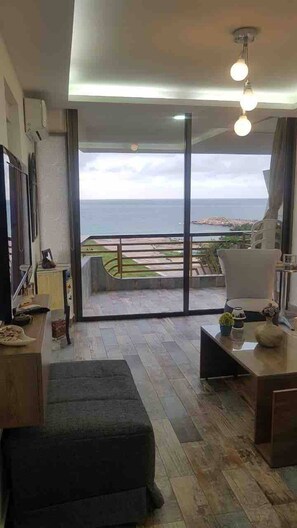 Sala de estar moderna com uma grande porta de vidro deslizante que dá para uma varanda com vista para o mar.