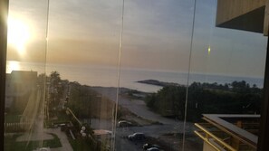 Vista pela janela com um pôr do sol, área de estacionamento e estrada que leva a um corpo d'água.