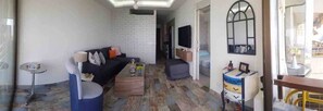 Sala de estar com sofá, mesa de centro, televisão e piso estampado.