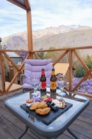 Uma mesa de vidro com comida e bebidas em um deck com vista para a montanha.