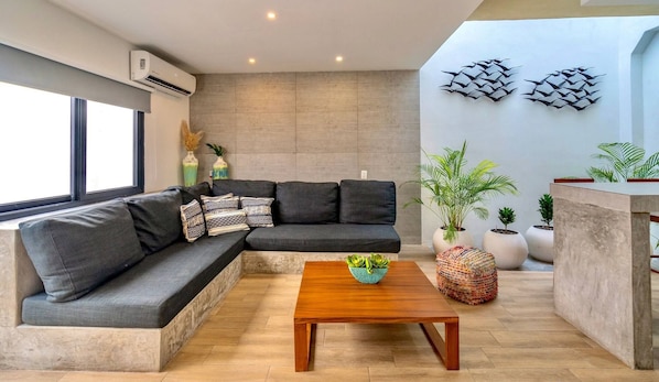 Uma sala de estar moderna com um sofá seccional, uma mesa de centro de madeira e plantas em vasos.