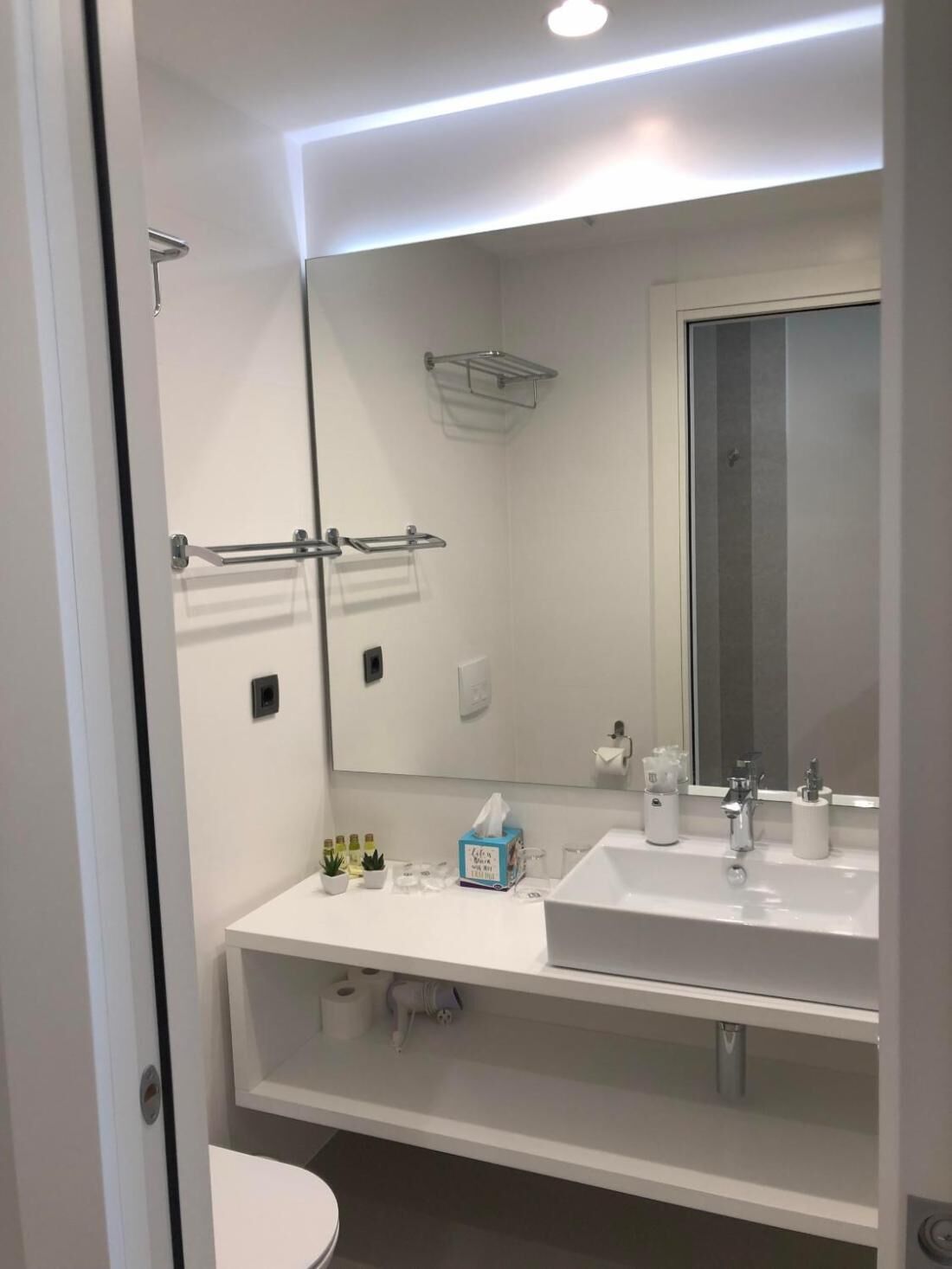 Uma casa de banho moderna com lavatório branco, espelho e suporte para toalhas.