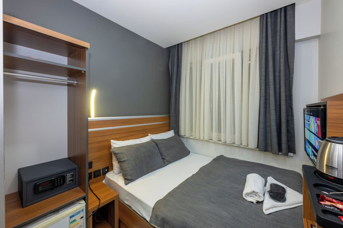 Quarto de hotel com cama, mesa de cabeceira com abajur, televisão, frigobar e guarda-roupa.