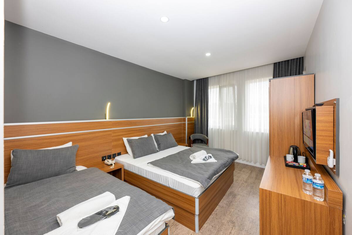 Quarto de hotel com duas camas, cabeceira de madeira, televisão, mesa com cafeteira e minibar.