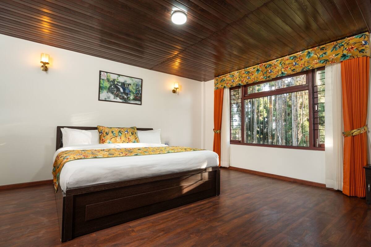 Quarto com cama de madeira, uma janela grande com cortinas e luminárias fixadas na parede.