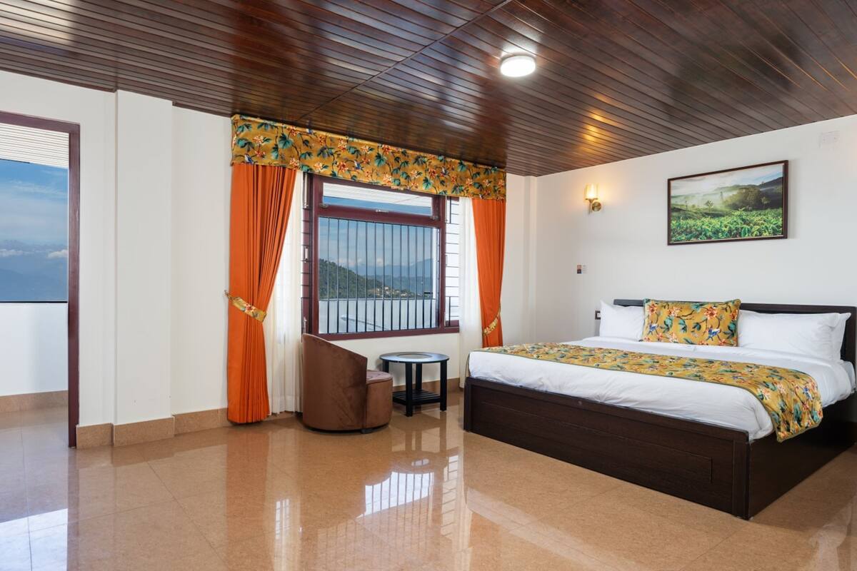 Quarto de hotel com cama, uma mesinha, uma cadeira e vista para as montanhas pela janela.