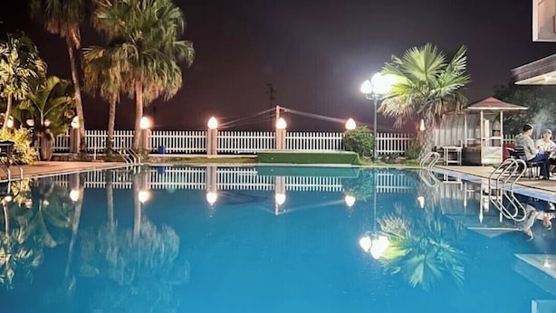 Piscina à noite com palmeiras e cerca branca.