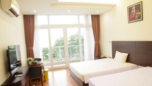 Quarto de hotel com duas camas, uma escrivaninha com cadeira, televisão e uma janela grande com cortinas.