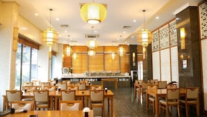 Restaurante com mesas e cadeiras de madeira, luminárias pendentes e um buffet central.