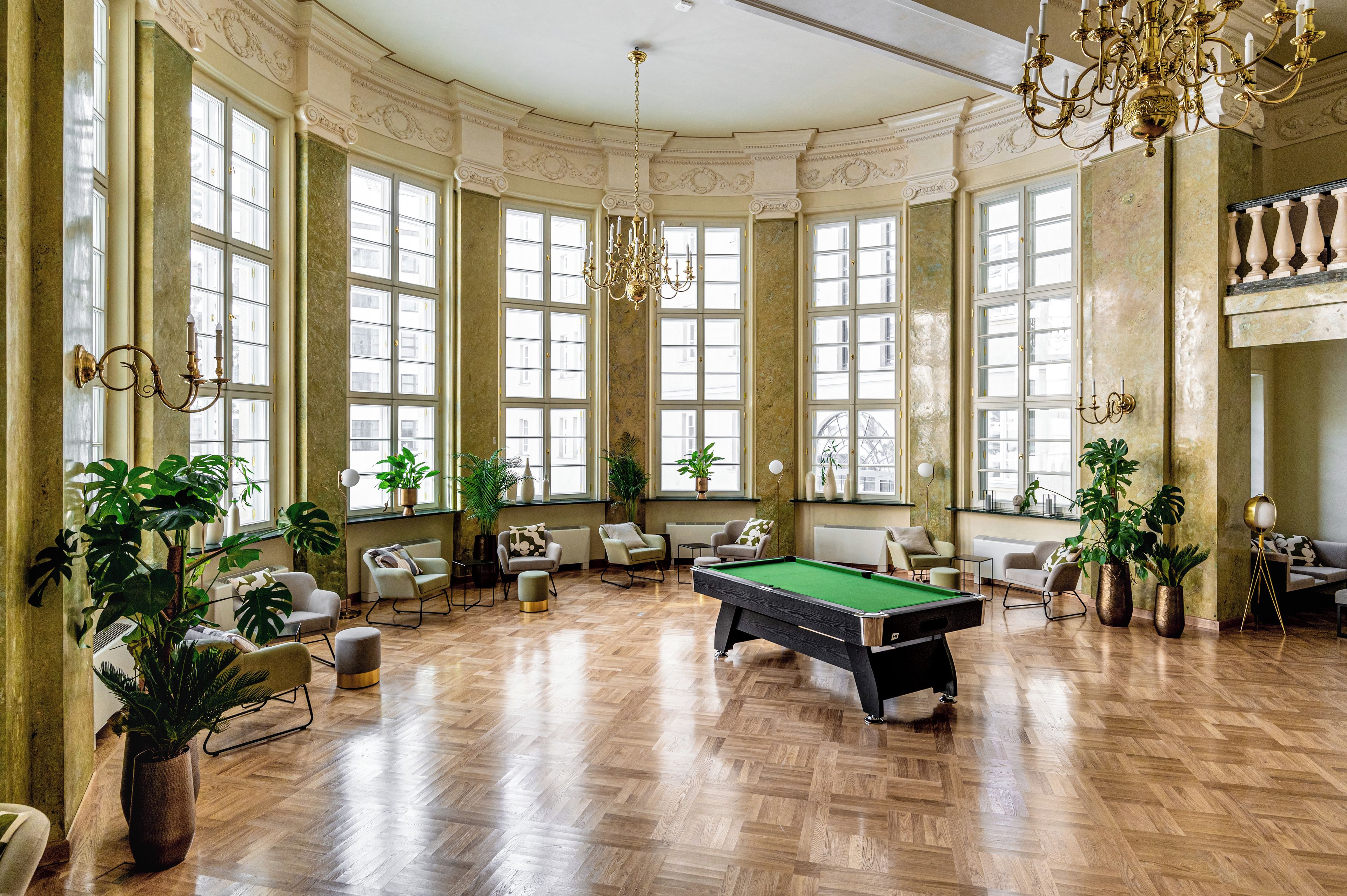 Um quarto espaçoso com mesa de bilhar, assentos confortáveis, janelas amplas e plantas decorativas.